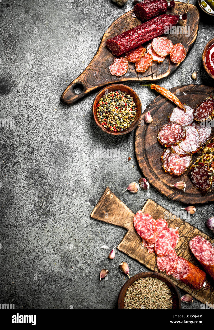 Different kinds of salami with spices and herbs on old boards. On a ...