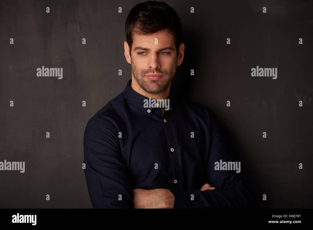 Thinking young man standing with arms crossed at dark background Stock ...