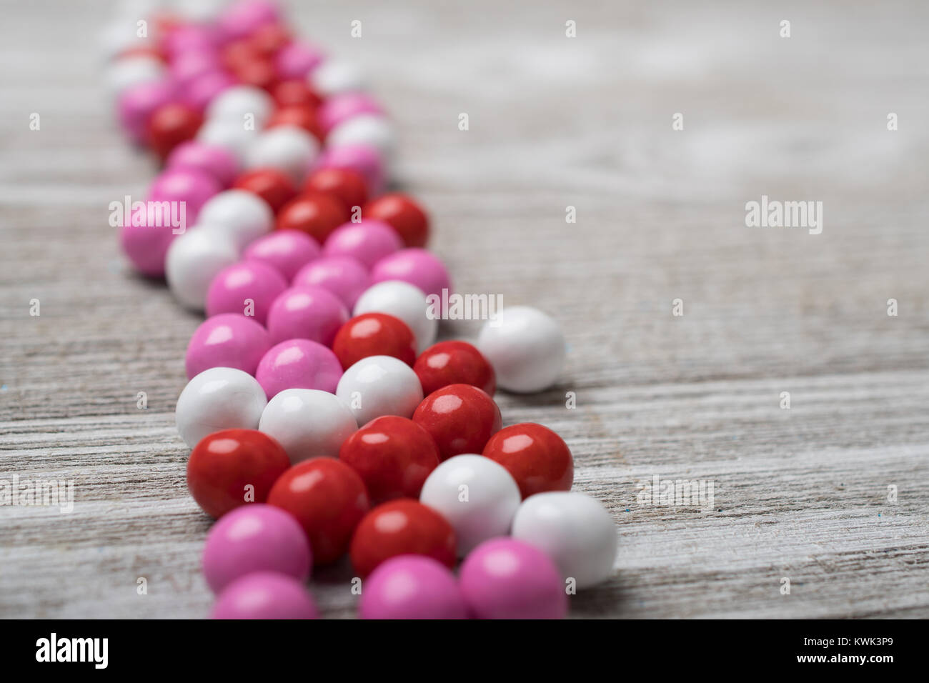 Red, pink and white candy scattered in a line on a white painted board ...