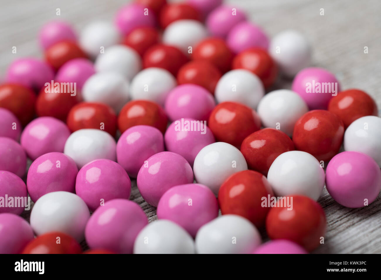 Pink, white and red round candies scattered on a white wooden board ...