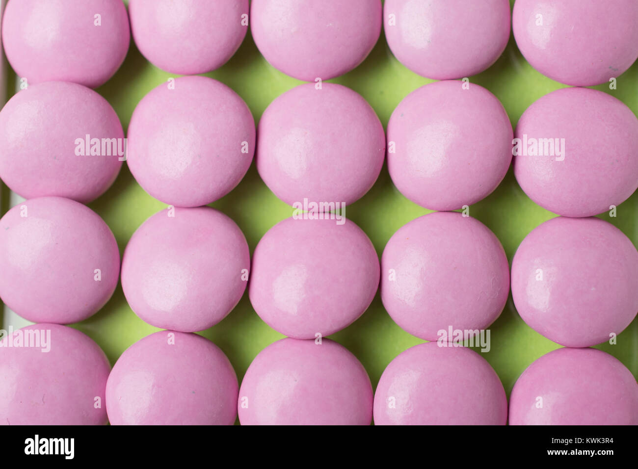Pink round candies arranged in lines with green background Stock Photo ...