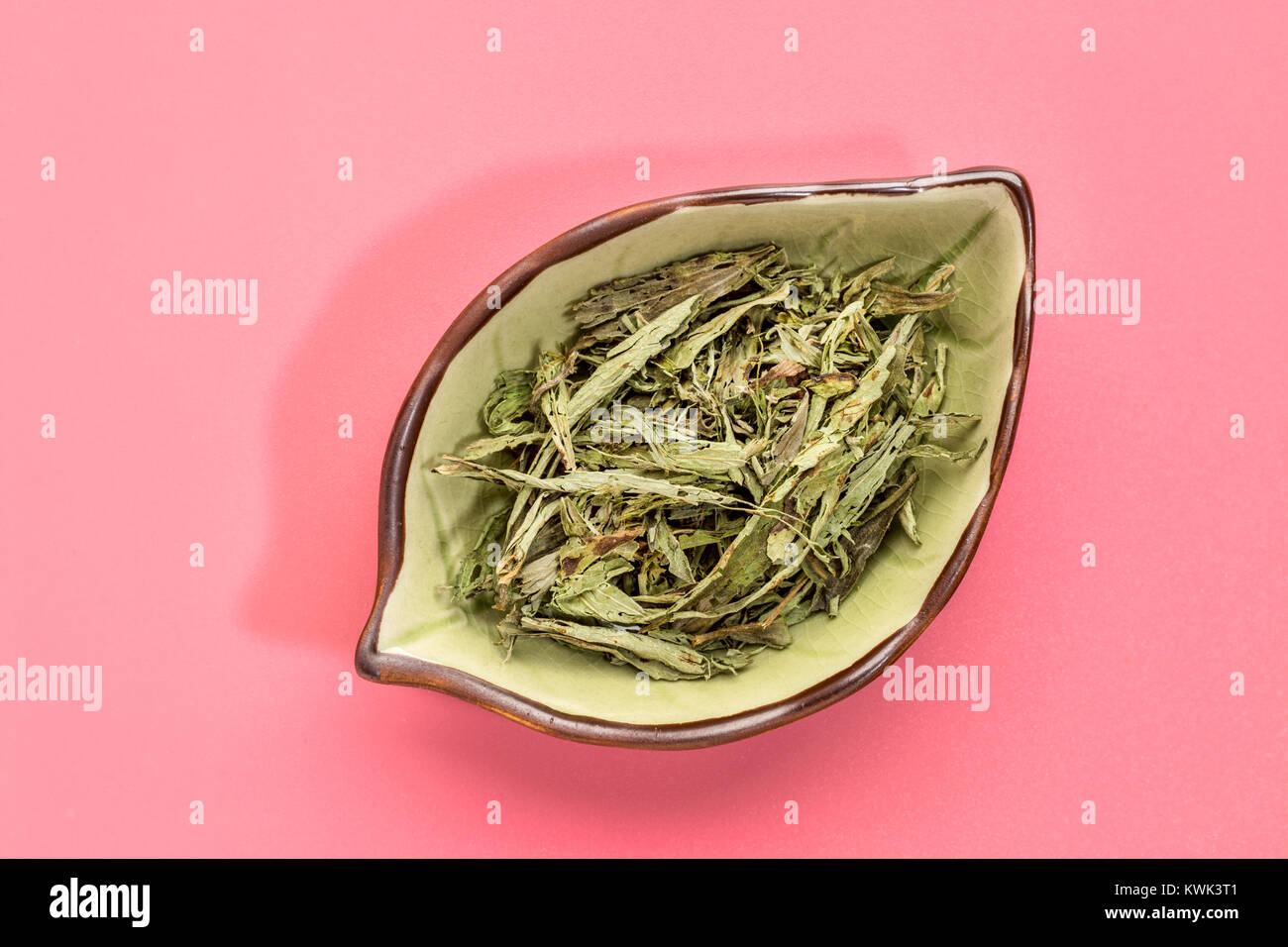 stevia dried leaves on ceramic leaf shape bowl against pink background ...