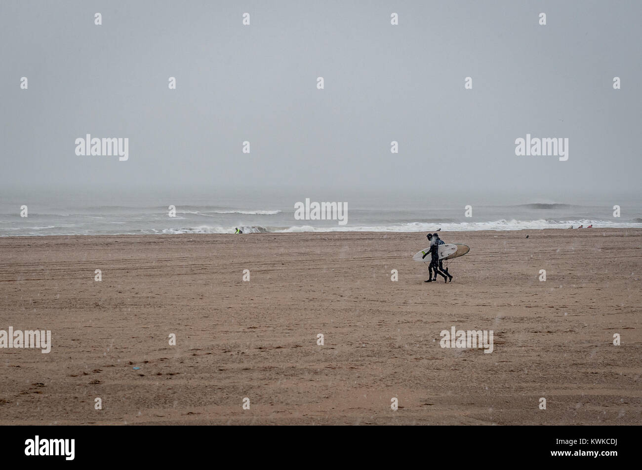 Surfers on a beach walking in the cold rain Stock Photo - Alamy