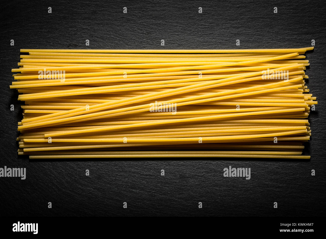 Bucatini pasta lies on a slate background. Lighting emphasises the ...