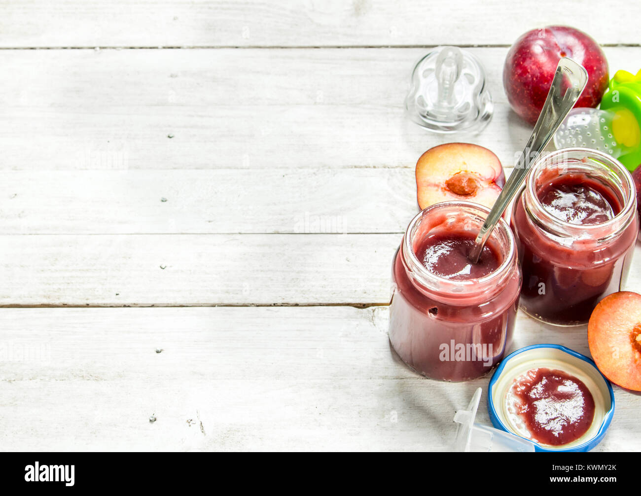 Baby food. Baby puree from fresh plum. On a white wooden background ...