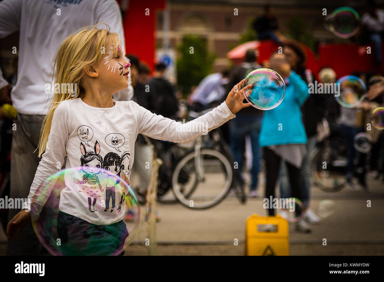 Young blond girl reaching out to touch an iridescent soap bubble ...