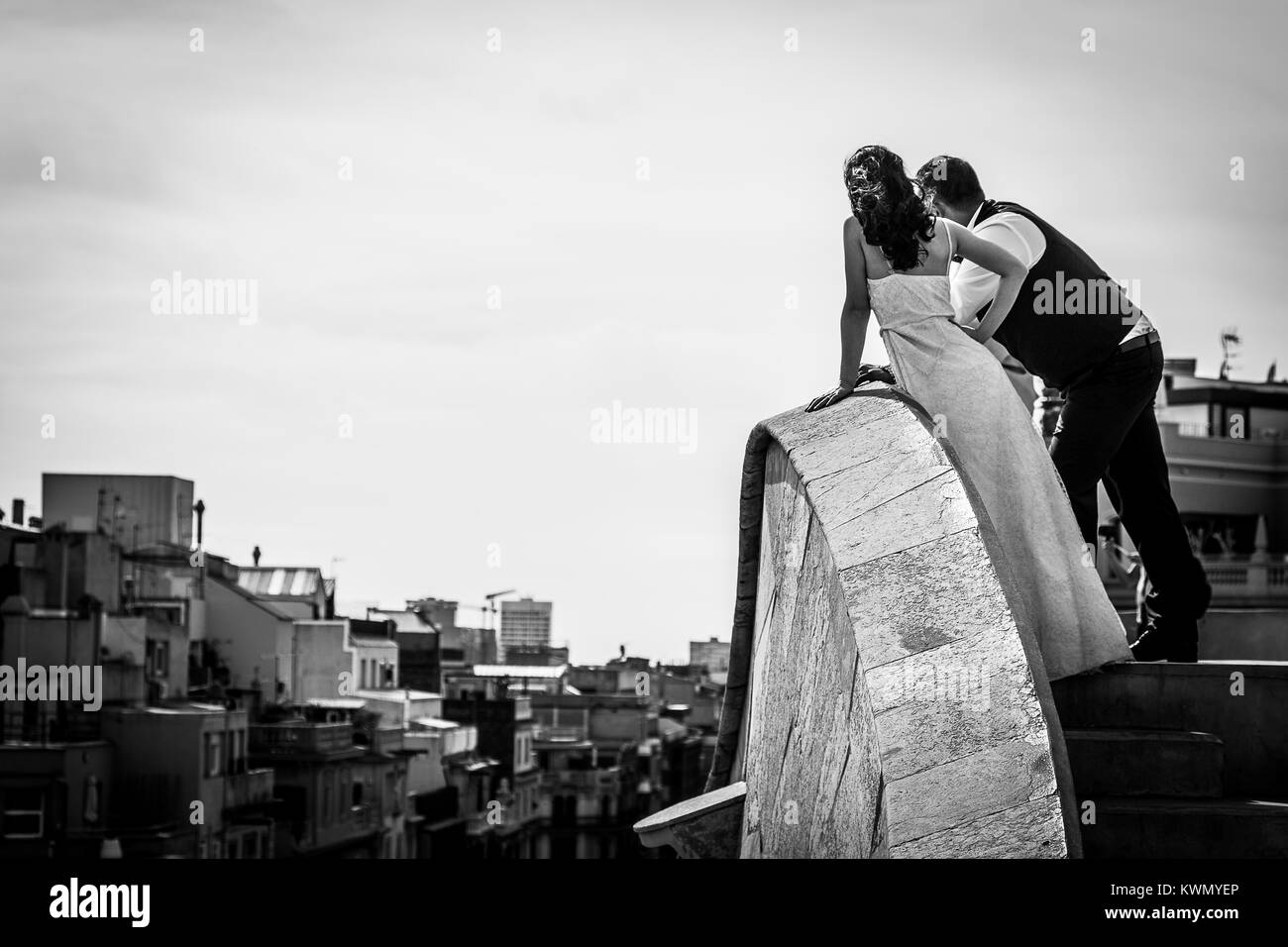 Black and white view of newlywed couple stood on roof looking over city ...