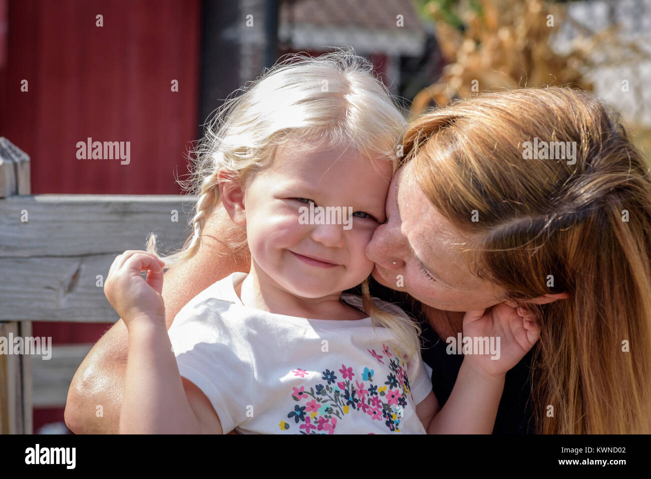 mother hugging and kissing child on cheek outside red barn in fall ...