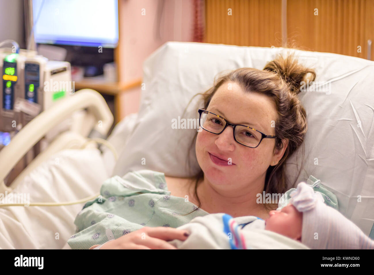 happy and tired new mom holding newborn baby in hospital bed after ...