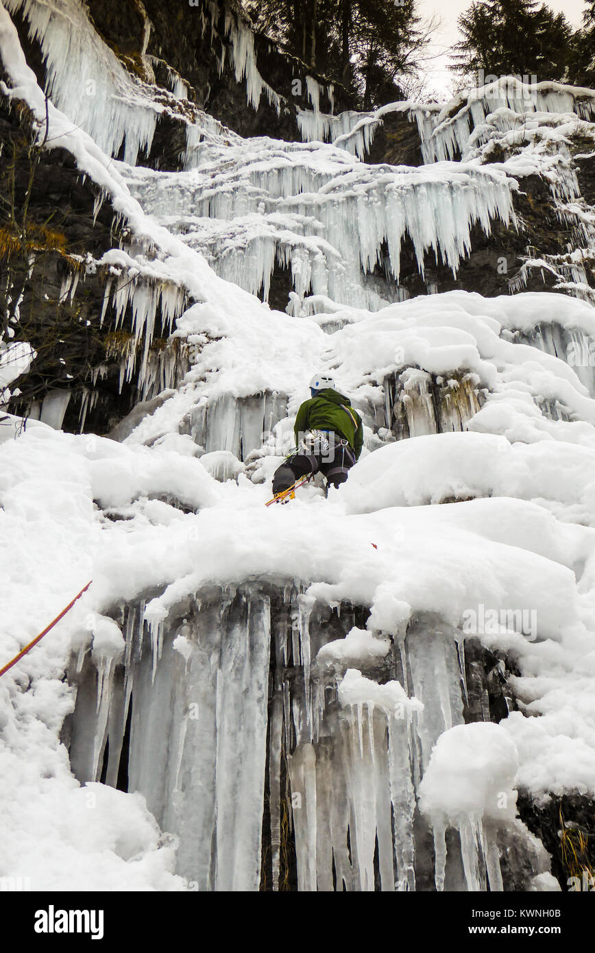 male ice climber in a green jacket on a frozen waterfall in the Swiss ...