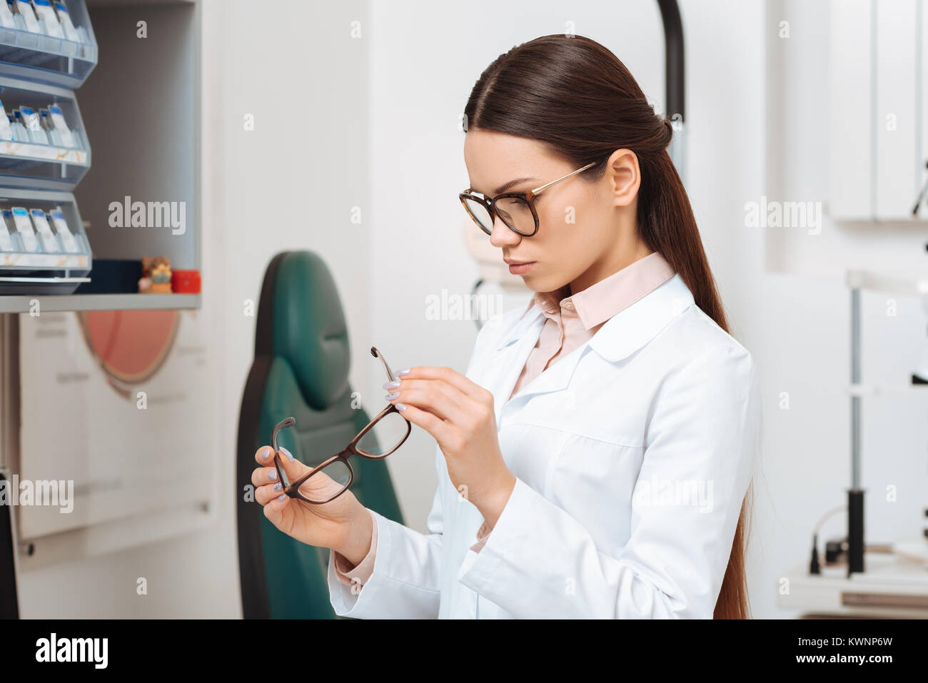 side view of focused ophthalmologist looking at pair of eyeglasses in ...