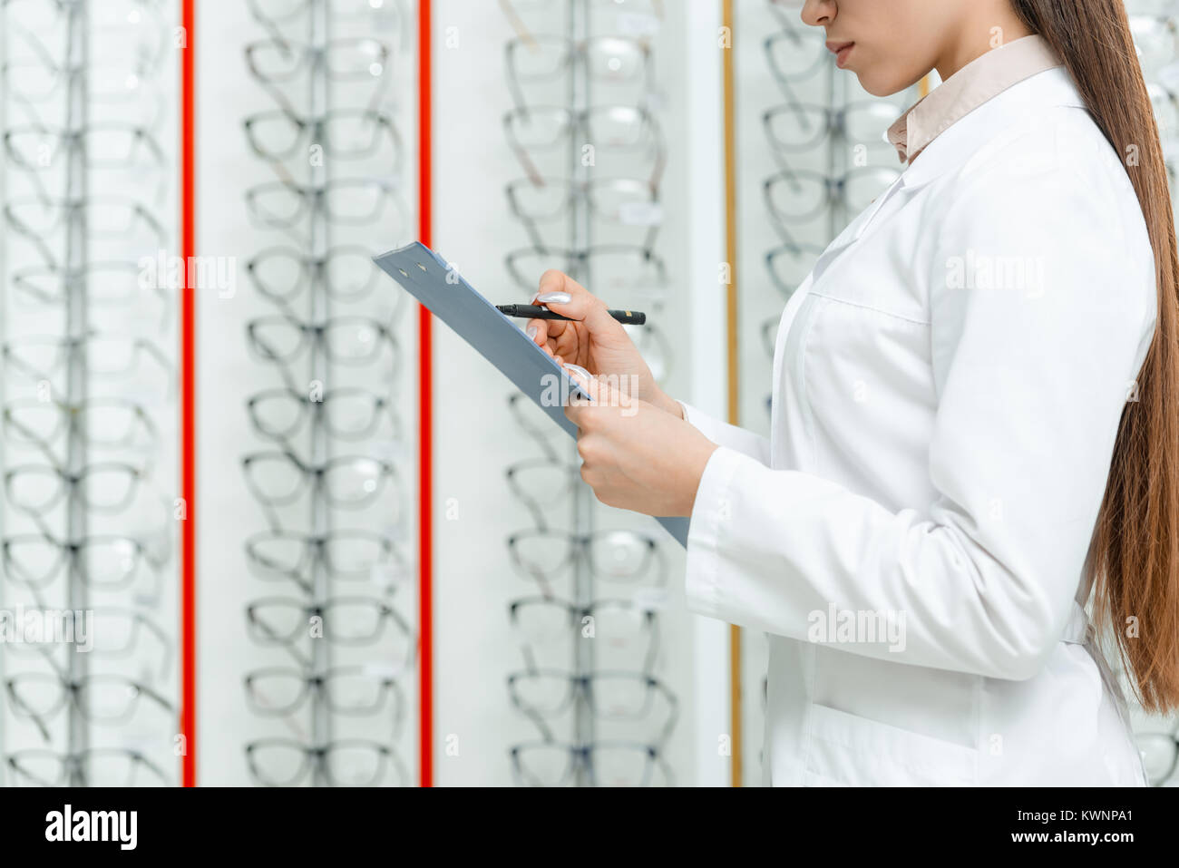 cropped shot of optometrist in white coat with notepad in hands ...