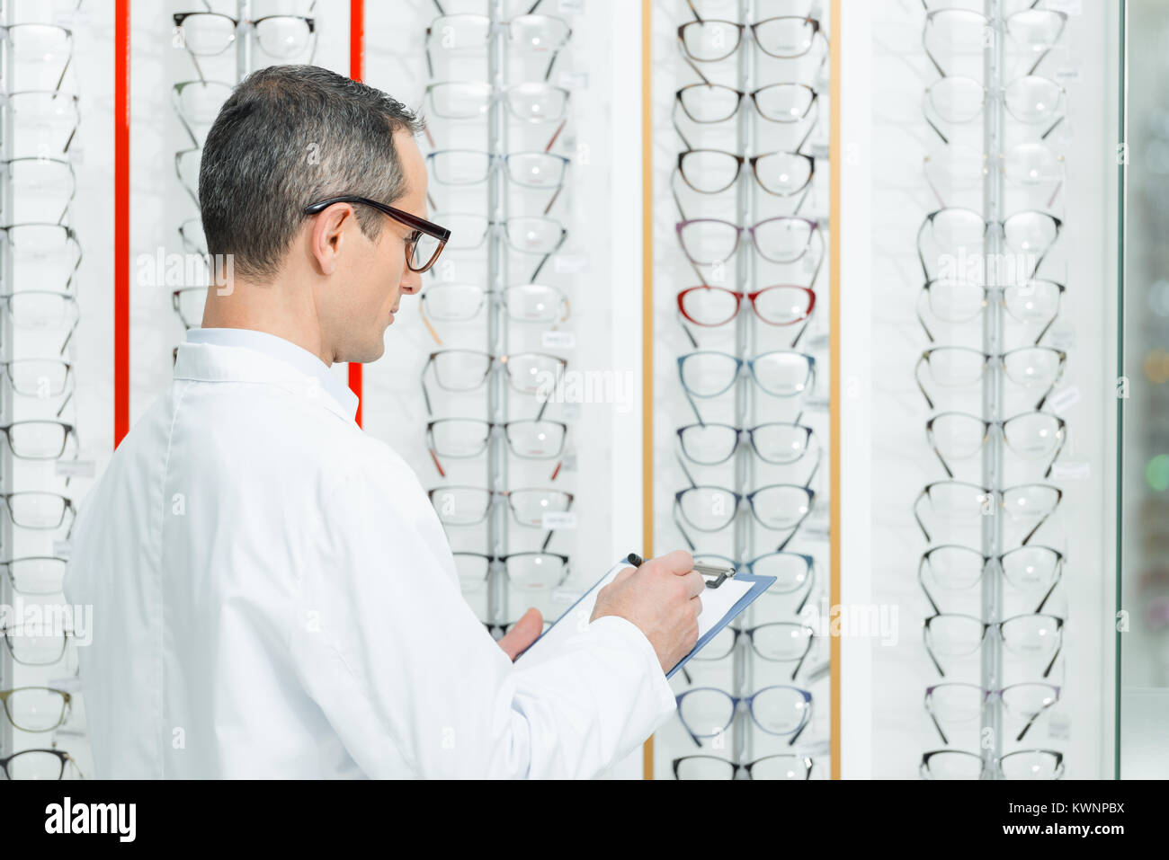 side view of optometrist making notes while standing at shelves with ...