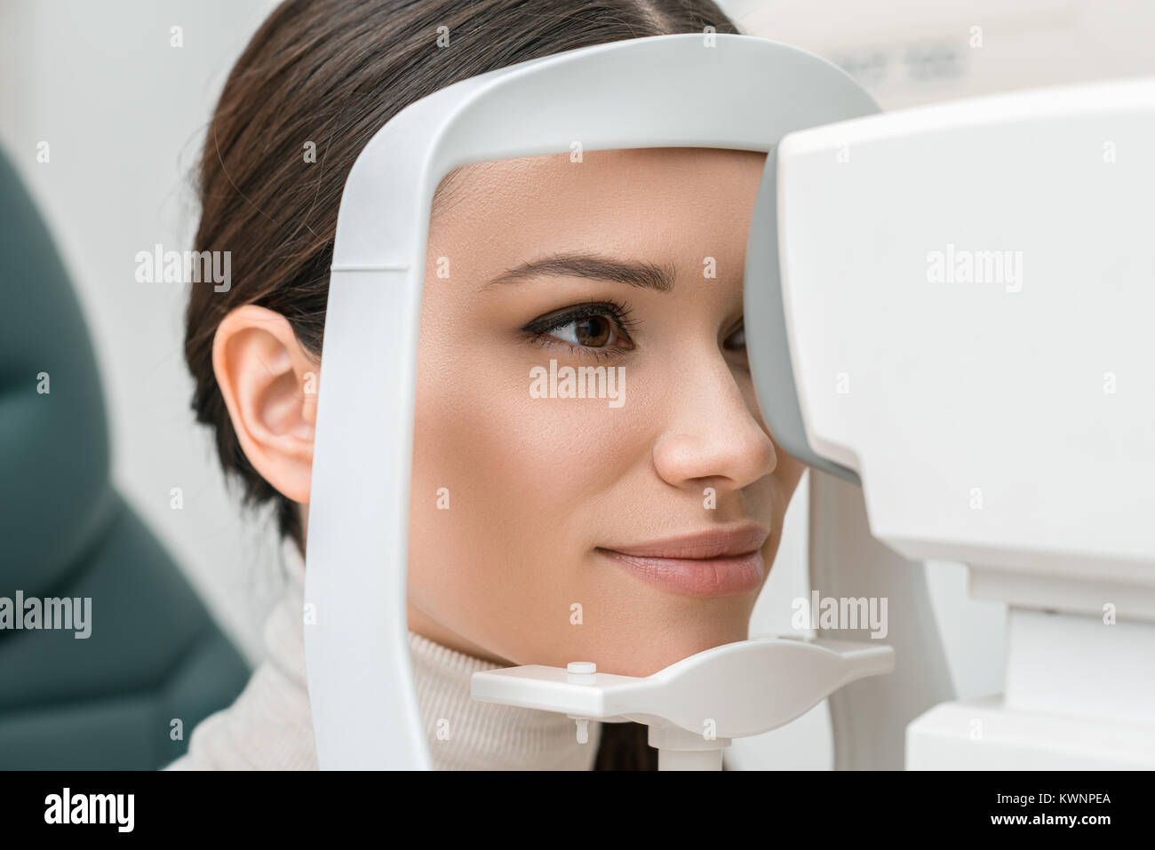 side view of young woman getting eye examination in slit lamp in clinic ...