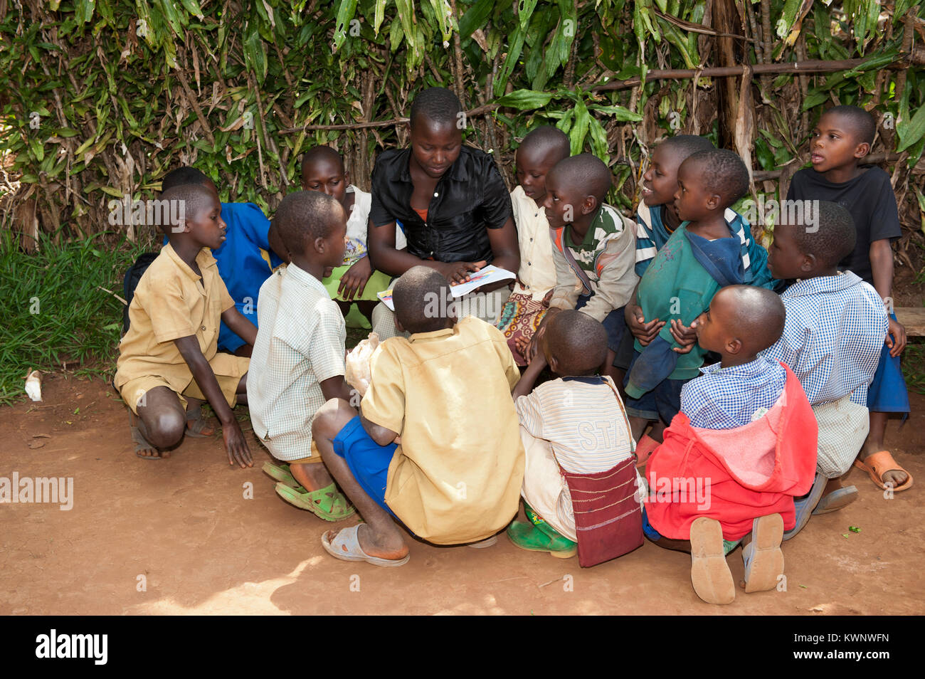 Young teacher reading a story to children gathered around her. Rwanda ...