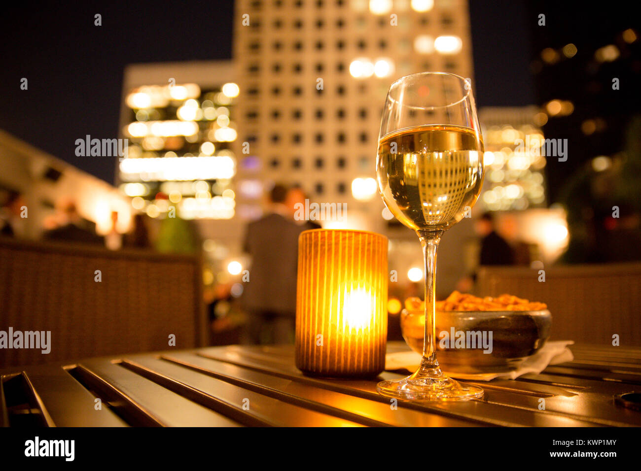 Glass of white wine and candle with evening view of city buildings ...