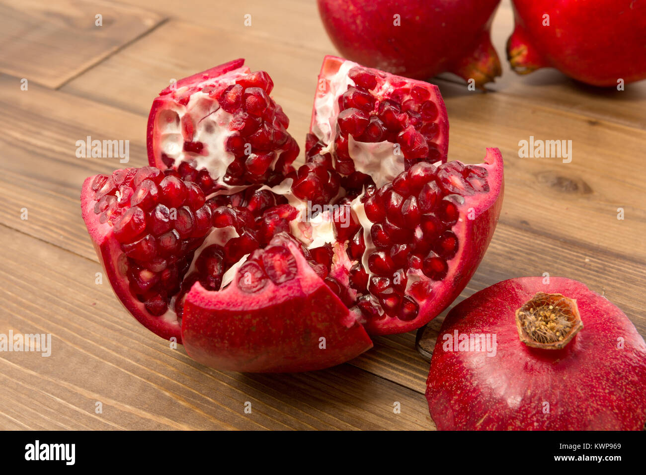 Closeup of two whole and one cut open pomegranates on a wooden table ...
