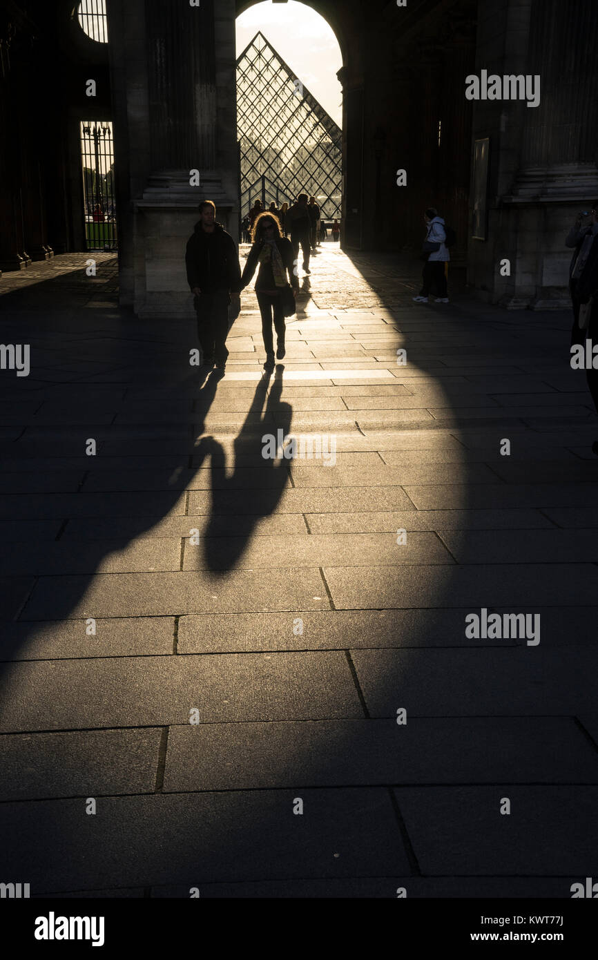 Back lit couple walking through passage in the Louvre with the Pyramid ...