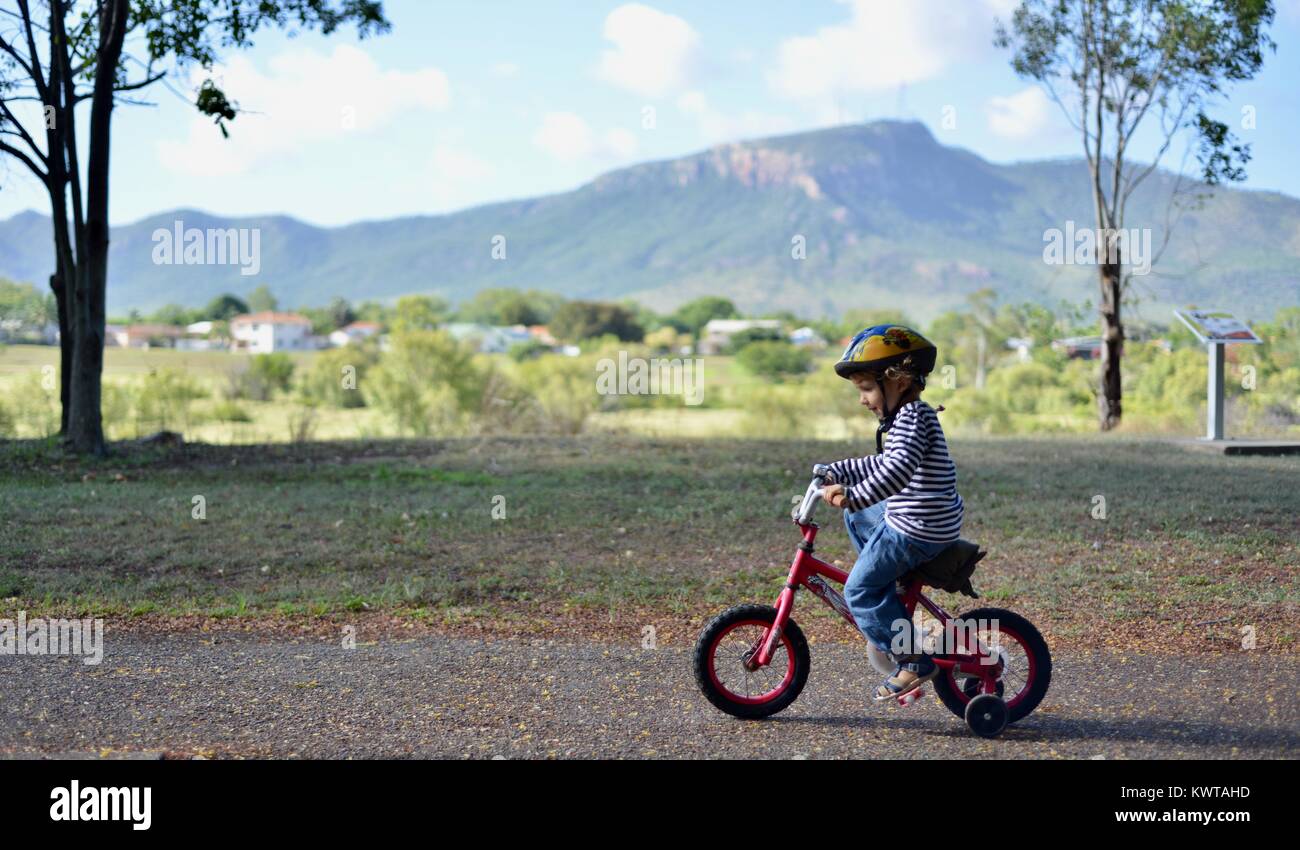 Small child riding a bicycle with training wheels along a path ...