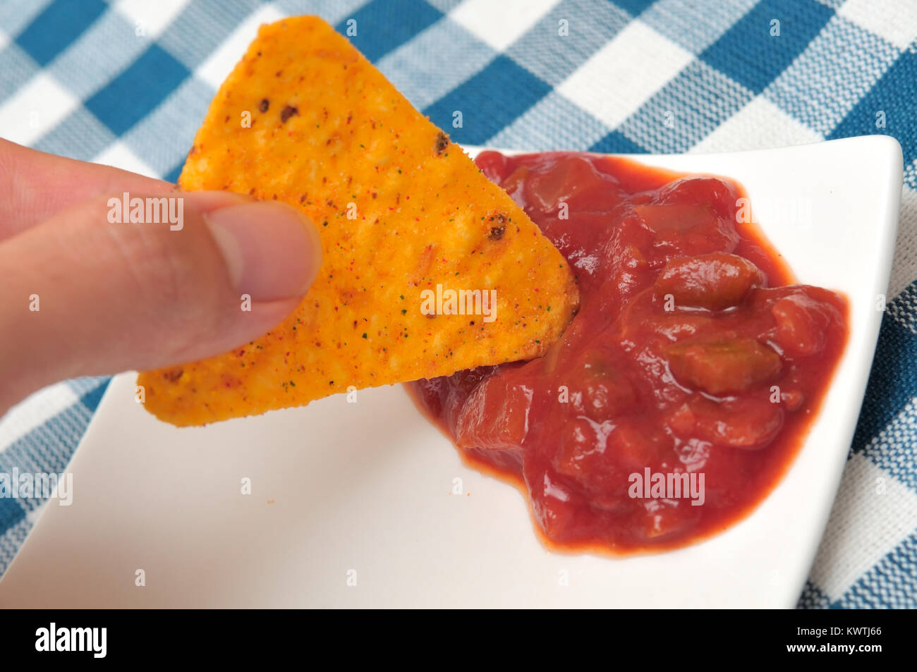 Dipping single tortilla chip into tomato sauce Stock Photo - Alamy
