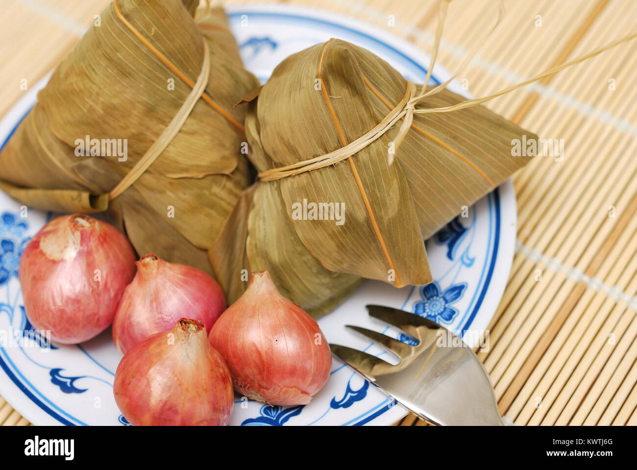 Traditionally wrapped rice dumplings and onions on plate Stock Photo ...