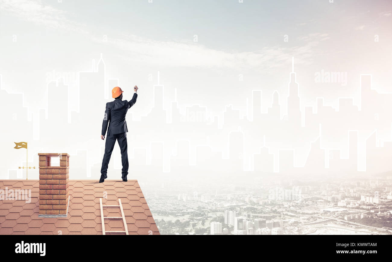 Engineer man standing with back on house roof and drawing city. Mixed ...