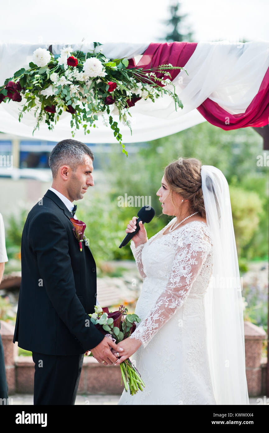 Wedding couple making vows outdoor under the floral arch in front of ...