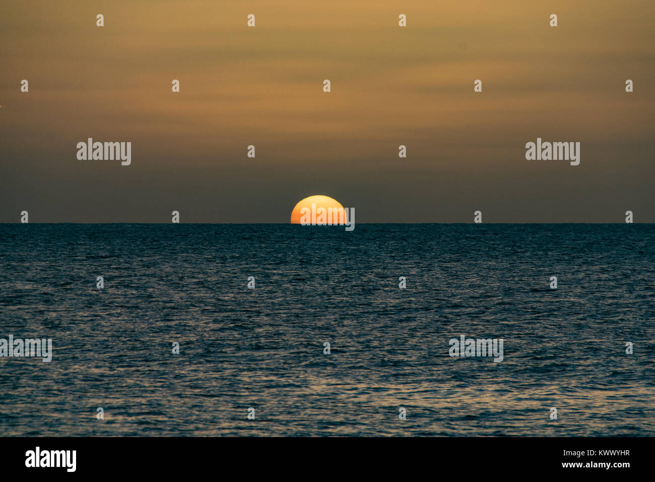 The setting sun over a still calm ocea Stock Photo - Alamy