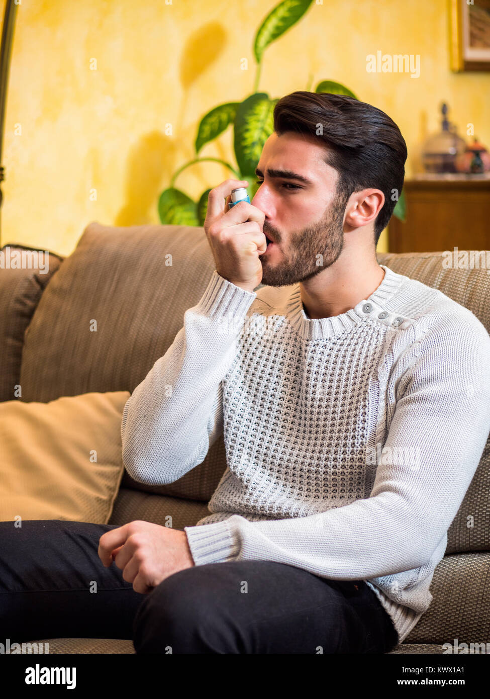 Handsome young man using inhaler for asthma, while sitting on sofa at ...