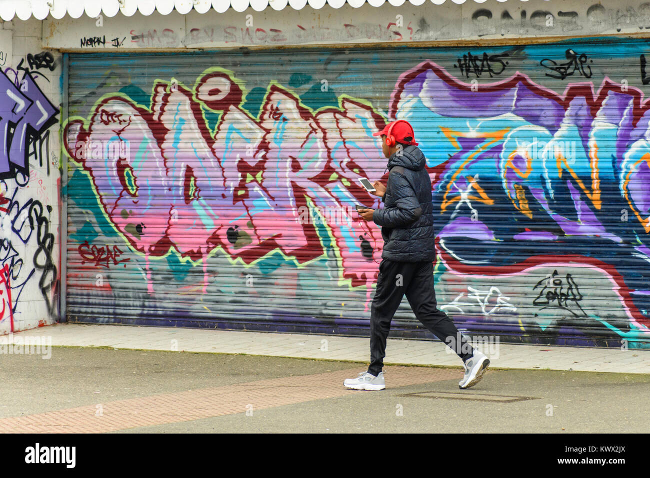 A young black male walking past brightly coloured graffiti sprayed on ...
