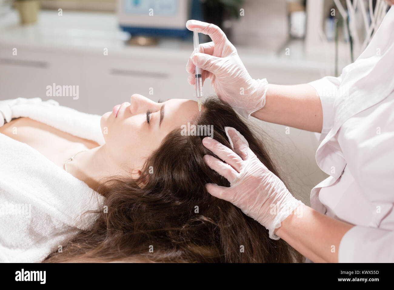 Handsome woman receives an injection in the head. The procedure makes ...
