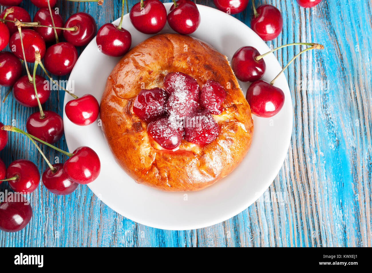Fresh homemade bun with sweet cherry in a white dish on a blue wooden ...