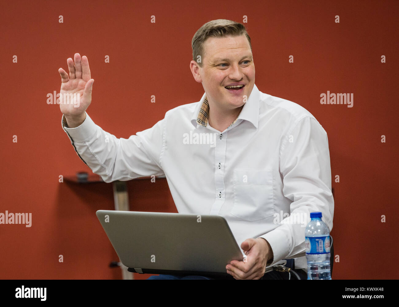 Businessman giving a seminar holding laptop with one hand raised Stock ...