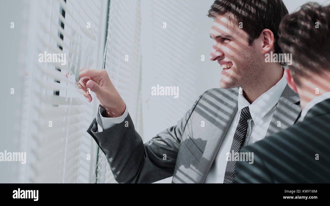 photo side view, smiling office staff pushes the curtain and looks out ...