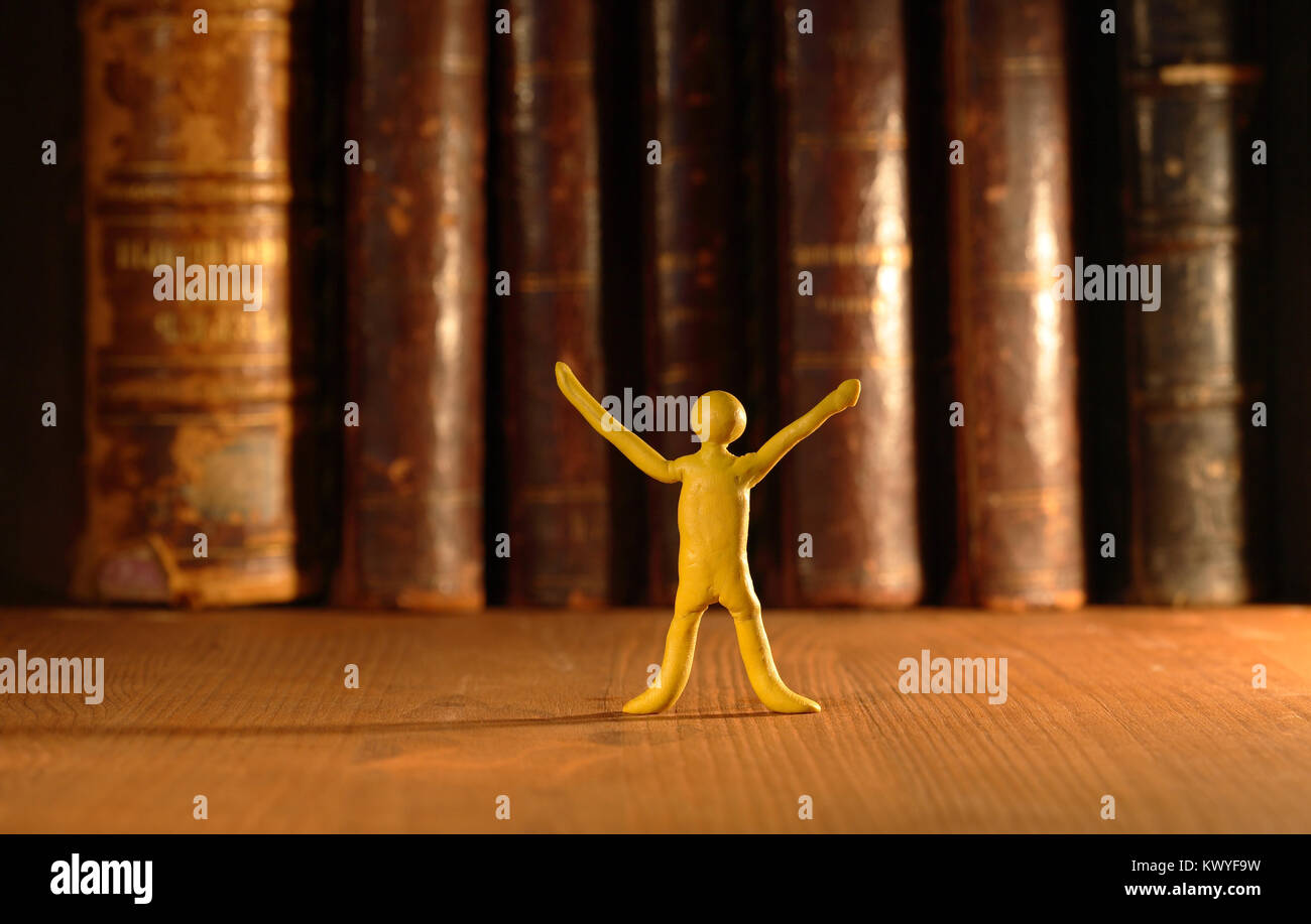 Small yellow plasticine man standing on background with old books in a ...