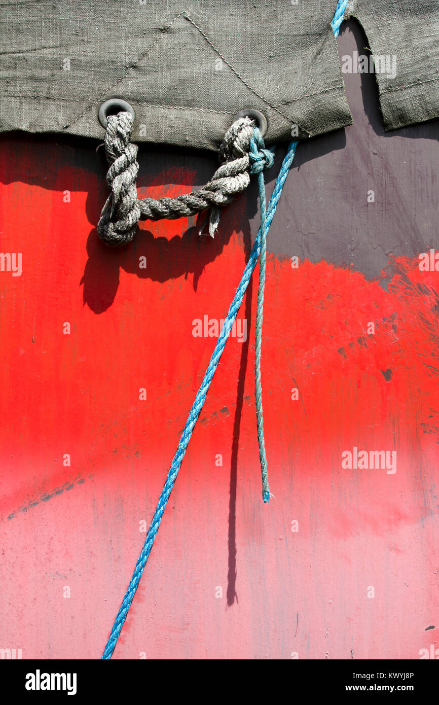 Grey tarpaulin with rope handle, tied with blue rope, over an old red ...