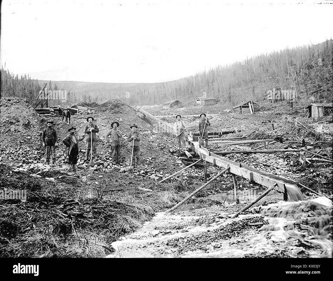 This photograph shows miners, a flume, and cabins at Hunker Creek ...
