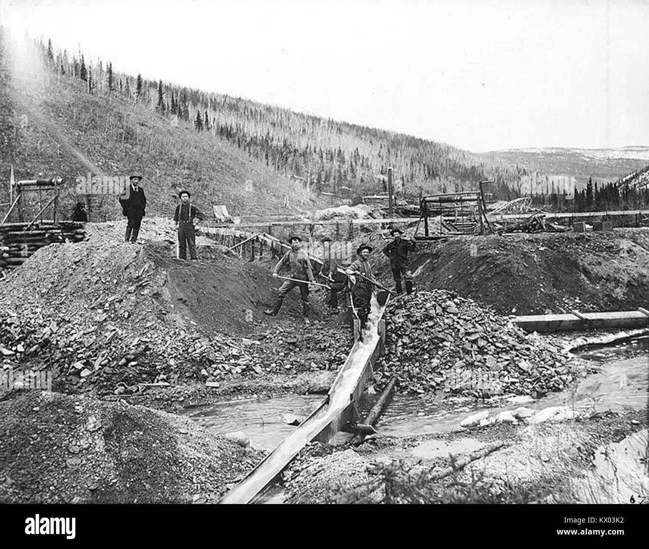 A historic image depicts six miners working beside a wooden flume at a ...