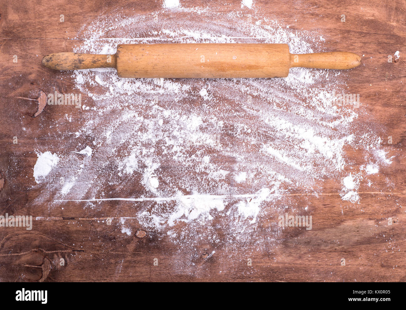 scattered flour on a brown wooden table, at the top a wooden rolling ...