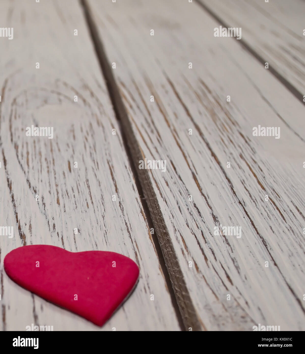 A close up of a small red heart laying on a white wooden table Stock ...