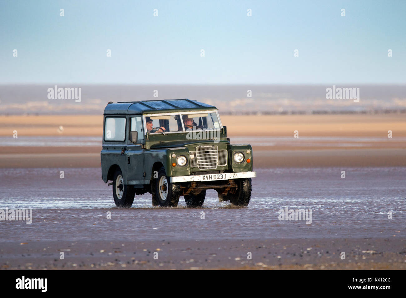 A classic British Land Rover being driven on the beach at Southport in ...
