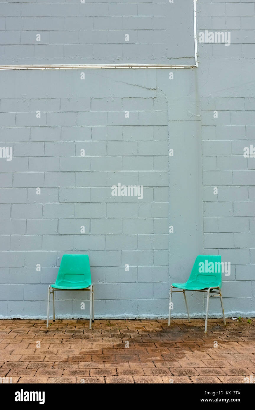 Two plastic chairs against a grey brick wall Stock Photo - Alamy
