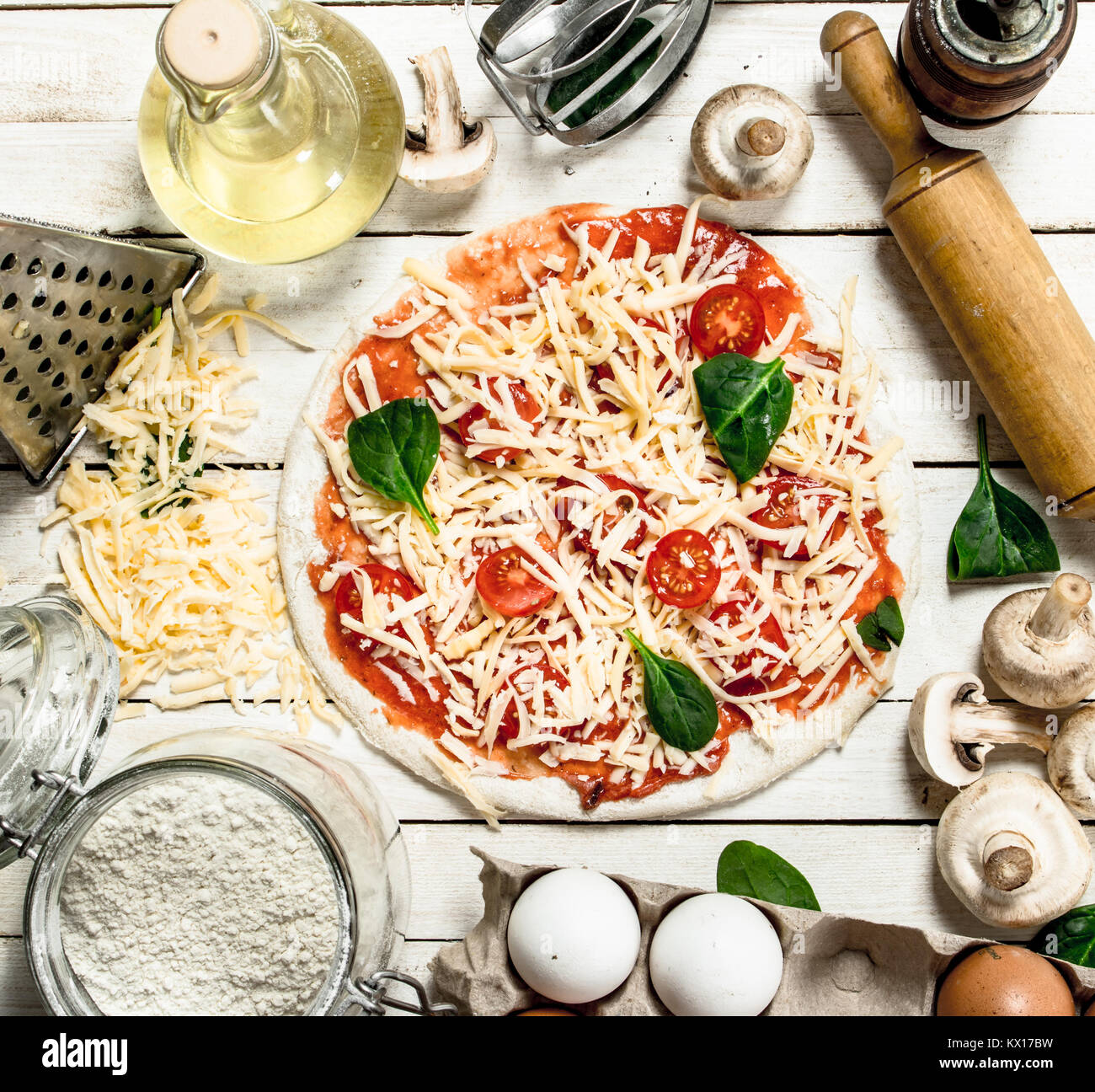Preparation of pizza with various ingredients. On a white wooden table ...