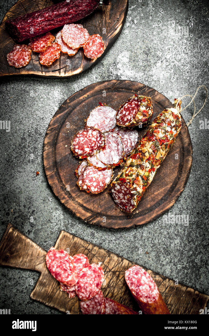 Different kinds of salami with spices and herbs on old boards. On a ...