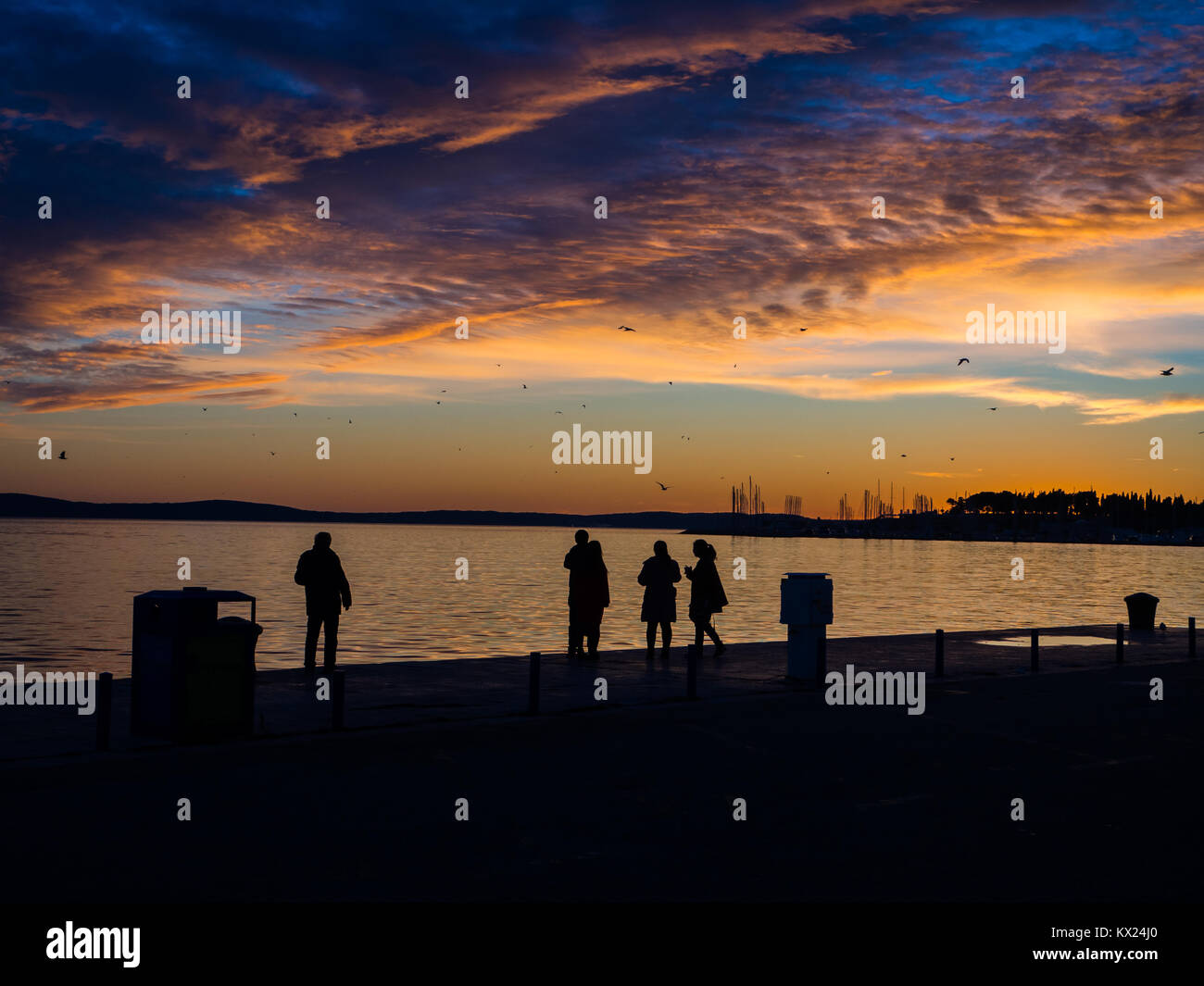 People standing by the sea and enjoying a beautiful colorful sunset ...