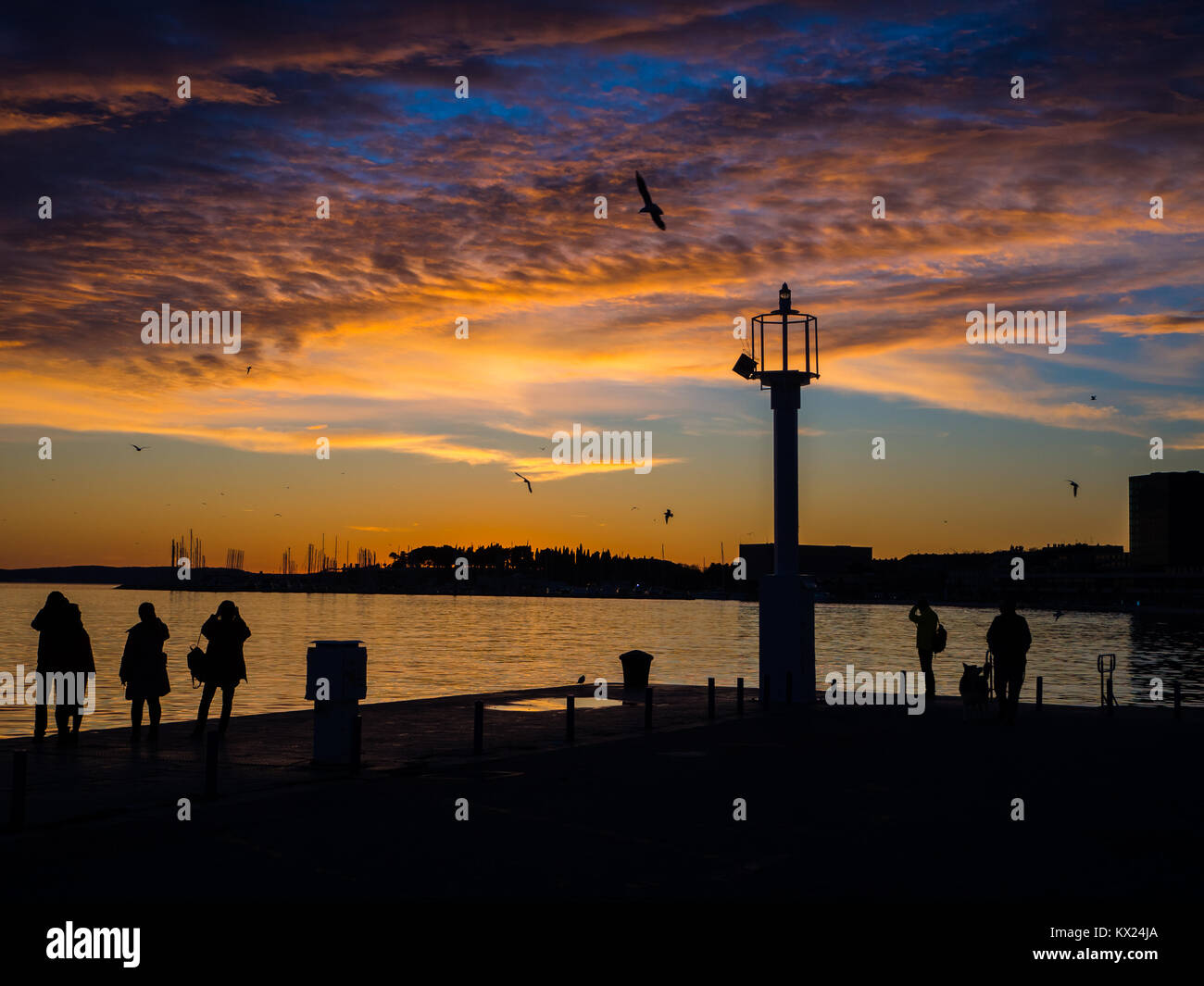 People standing by the sea and enjoying a beautiful colorful sunset ...