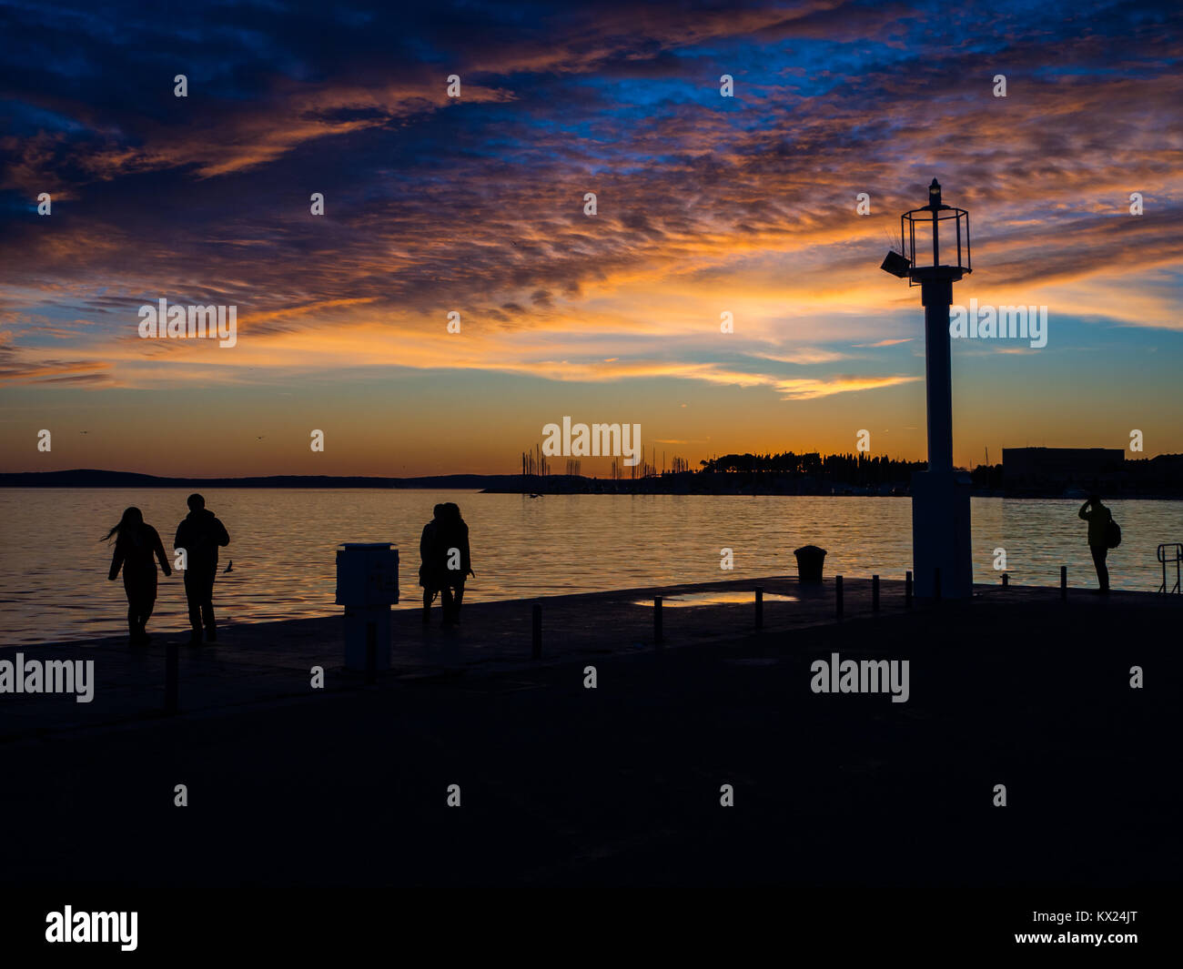 People standing by the sea and enjoying a beautiful colorful sunset ...