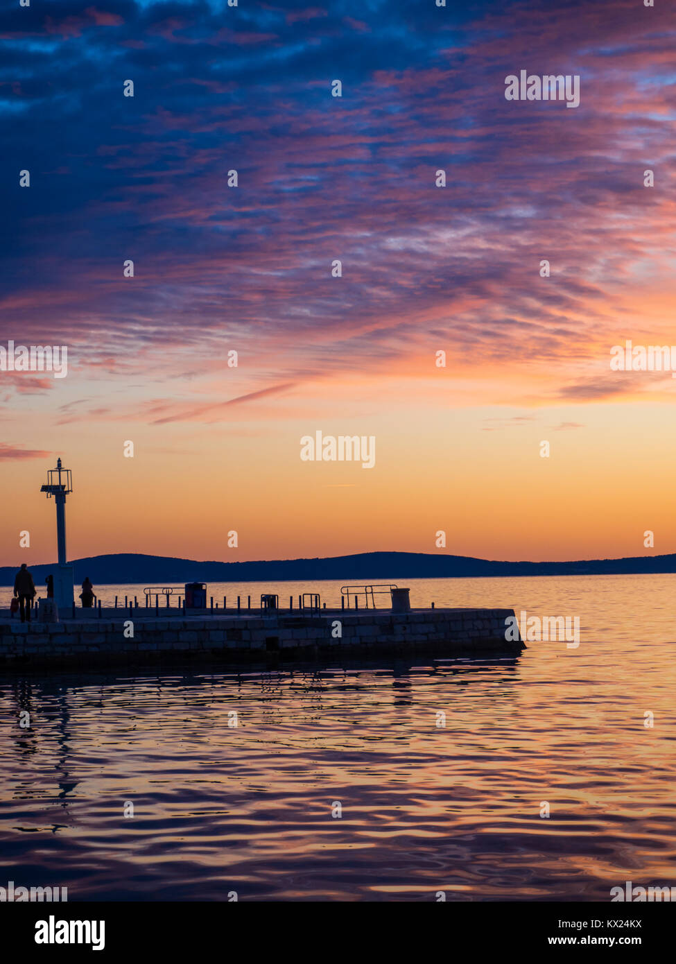People standing by the sea and enjoying a beautiful colorful sunset ...