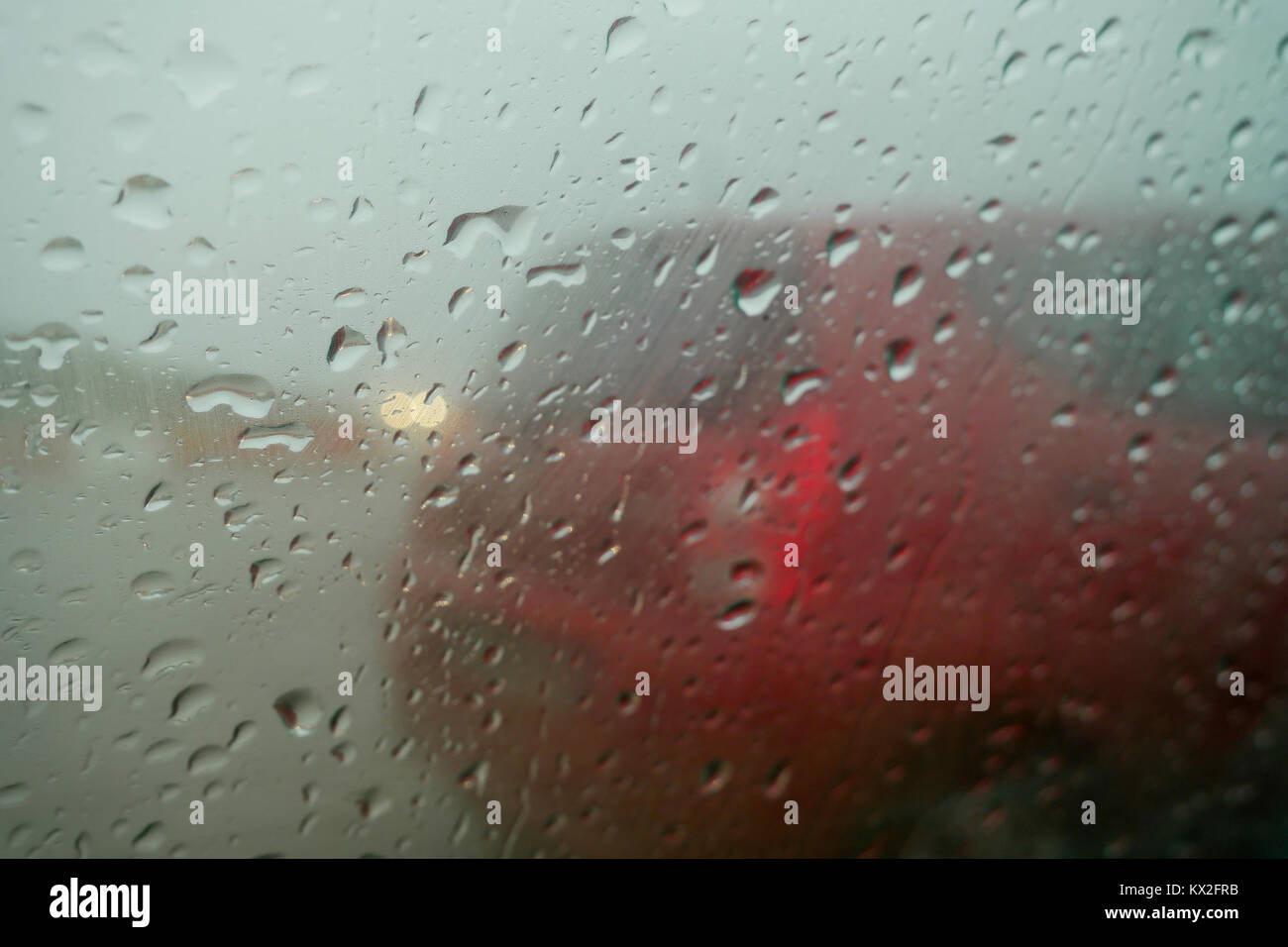 Red car seen through a rain drops covered car glass, Normandy, France ...