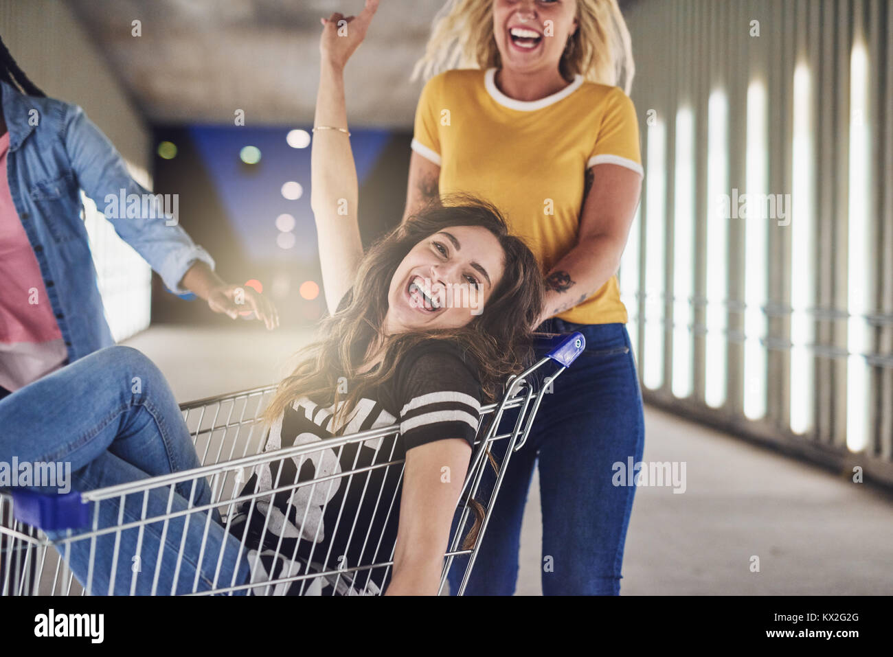 Two laughing young friends pushing their girlfriend down a walkway in ...